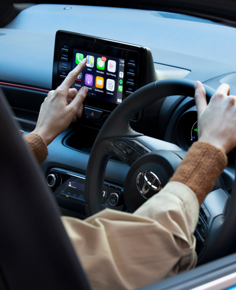 A woman sits behind the steering wheel of her Toyota, operating Apple ...